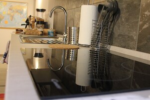Uma cozinha com pia de aço inoxidável, cafeteira, suporte para toalhas de papel e uma prateleira de metal.