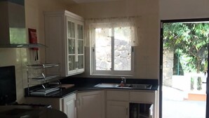 Uma cozinha compacta com armários brancos, bancada preta e janela com vista para uma parede de pedra.