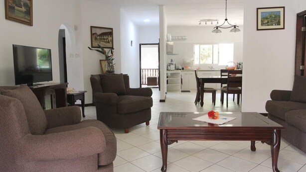 Uma sala de estar com sofás, uma mesa de centro, uma TV e um espaço de jantar com cadeiras e uma mesa.