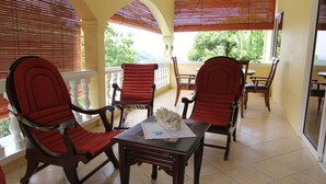 Varanda com três cadeiras vermelhas estofadas e uma mesa pequena, com um objeto decorativo no centro.