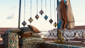 Terraço no telhado com um candeeiro suspenso, um sofá estampado e um grande toldo.