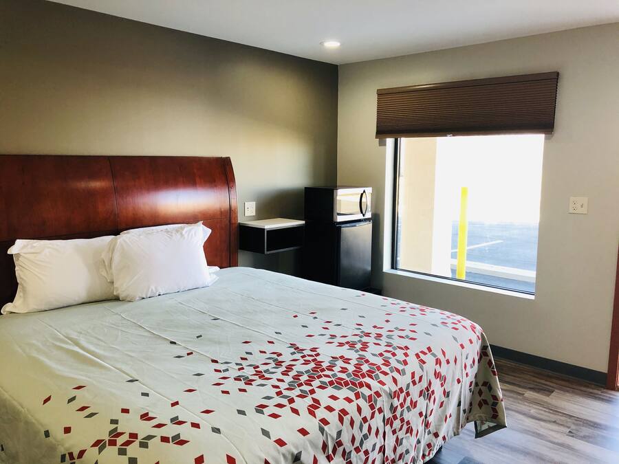 Quarto de hotel com cama grande, cabeceira de madeira, mesa de cabeceira pequena, televisão integrada e janela com vista.