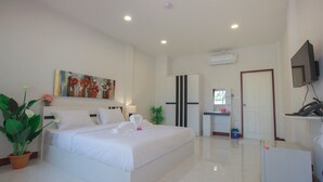 Quarto de hotel com uma cama grande, um quadro acima da cama, uma mesa com uma cadeira, uma TV na parede e um ar condicionado.