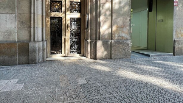 Entrada de edifício com portas de metal elaboradas e pavimento em mosaico.
