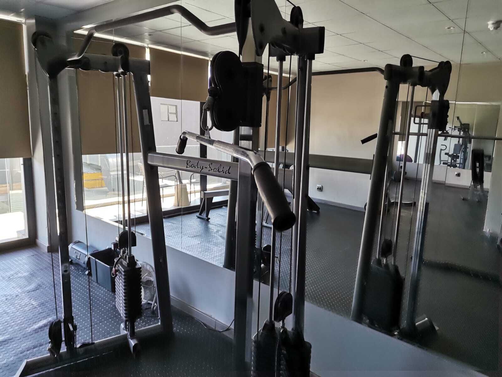Uma academia com equipamentos de cardio, aparelhos de musculação e um espelho grande na parede.