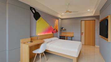 Quarto de hotel moderno com cama, escrivaninha, cadeira e televisão.