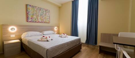 Quarto de hotel bem organizado com cama, mesas de cabeceira, escrivaninha e uma cadeira.
