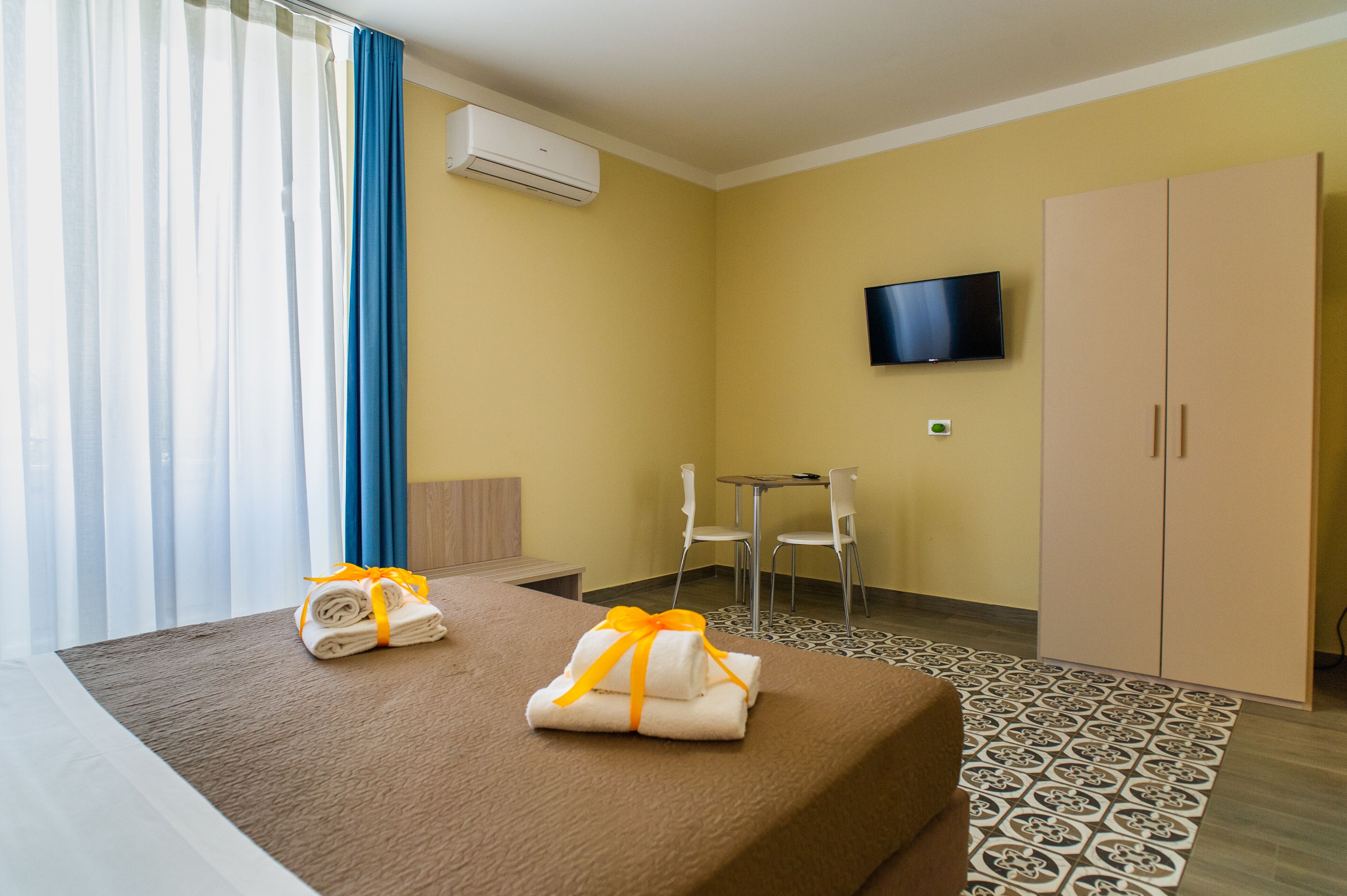Quarto de hotel com cama, escrivaninha, televisão e guarda-roupa.