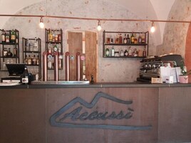 Uma área de bar com balcão, prateleiras com garrafas de bebidas alcoólicas, uma máquina de café e uma placa com a inscrição 'Accassi'.