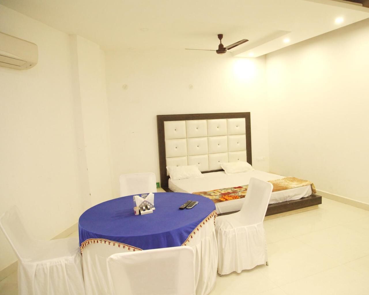 Quarto de hotel com cama, mesa redonda com cadeiras, ventilador de teto e ar condicionado.