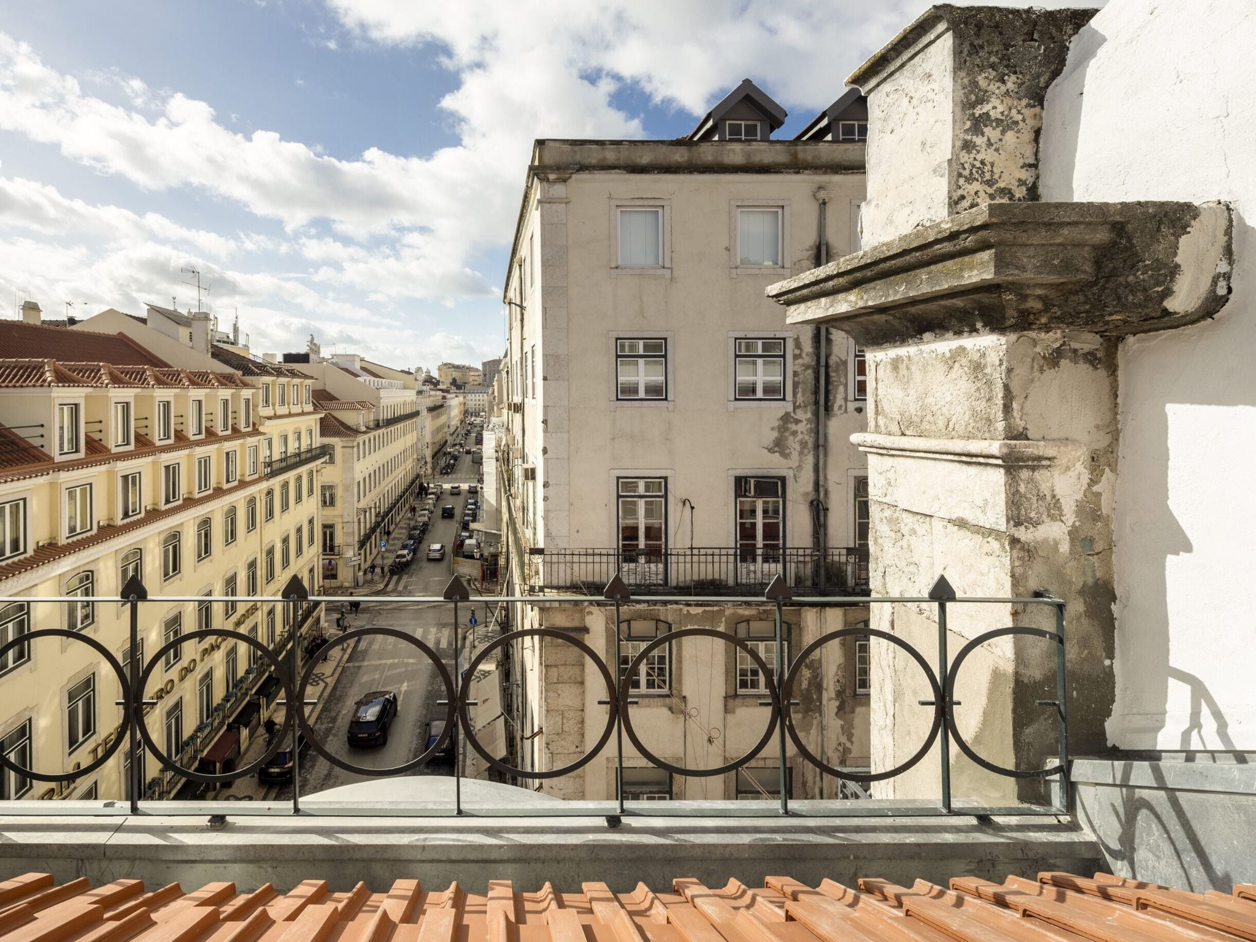 Vista de uma varanda com vista para uma rua com edifícios, escadas e grade de metal.