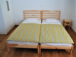 Uma cama de casal com estrutura de madeira e colcha amarela estampada.