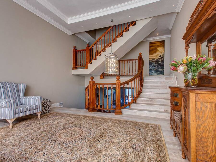 Uma sala ampla com um tapete estampado grande, uma poltrona listrada, uma escada de madeira e um armário de madeira.