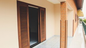 Um corredor com porta e persianas de madeira, um pilar de tijolo e chão ladrilhado.