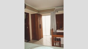 Quarto com cama, guarda-roupa de madeira, mesa de jantar com cadeiras e porta de vidro que dá para uma varanda.