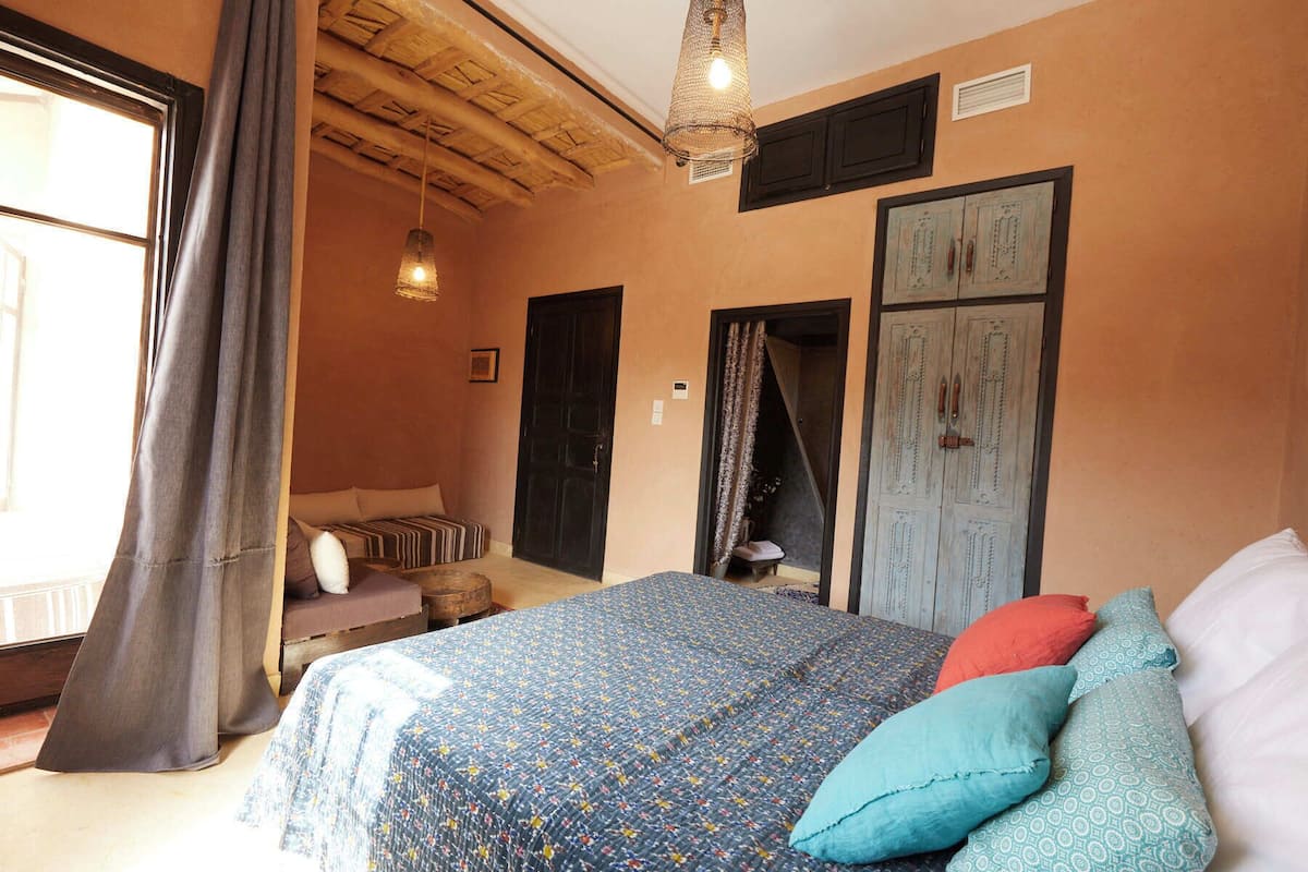 Um quarto com uma cama, uma janela com cortinas, teto de madeira e um guarda-roupa.
