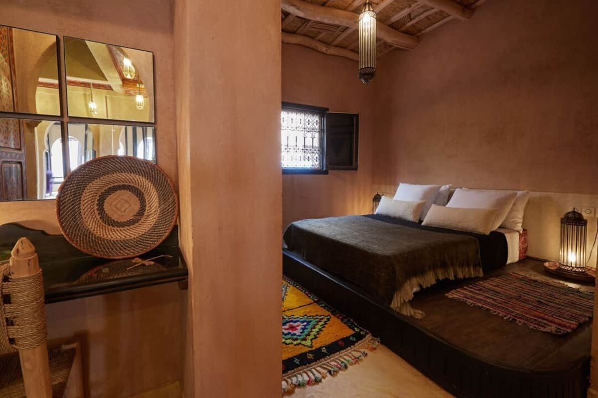 Quarto com cama, cesta de vime, abajur e janela com grade decorativa.