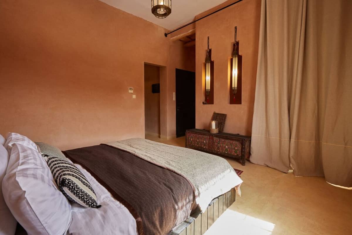 Quarto com cama, almofadas, cómoda e arandelas.