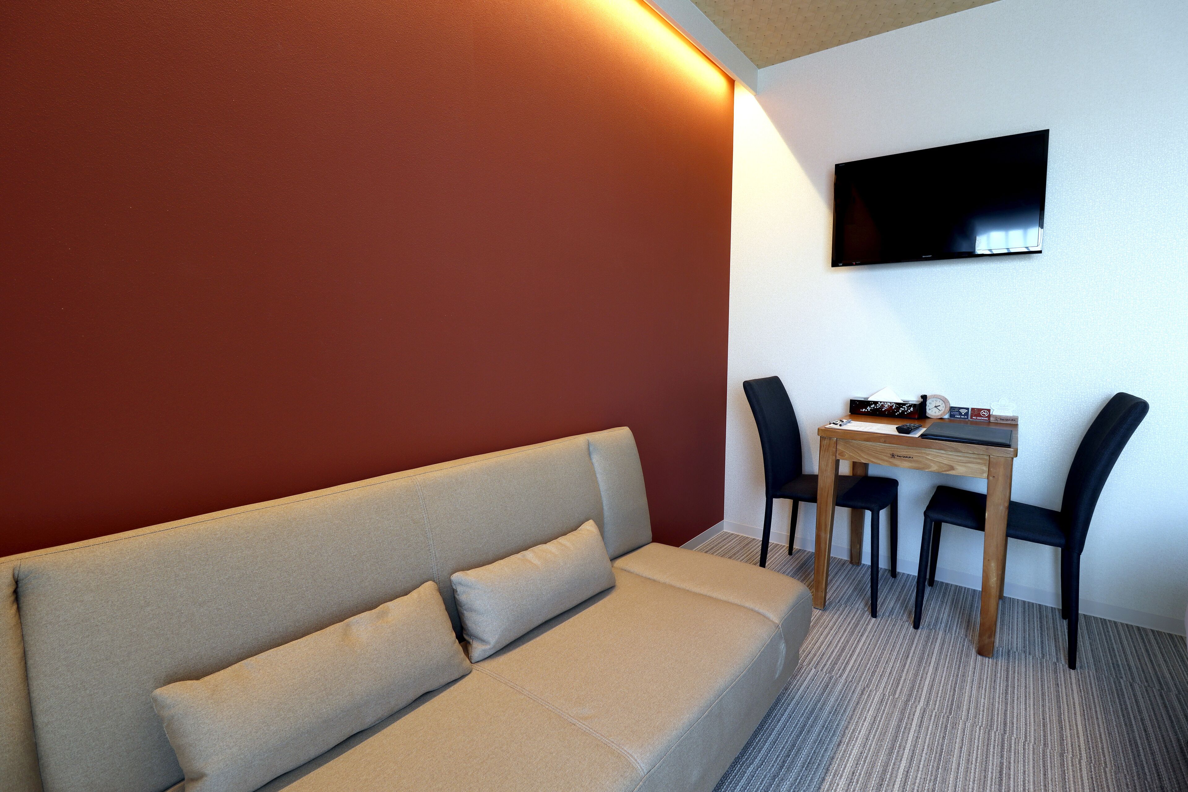 Quarto moderno com sofá, escrivaninha de madeira, duas cadeiras e TV de tela plana fixada na parede.