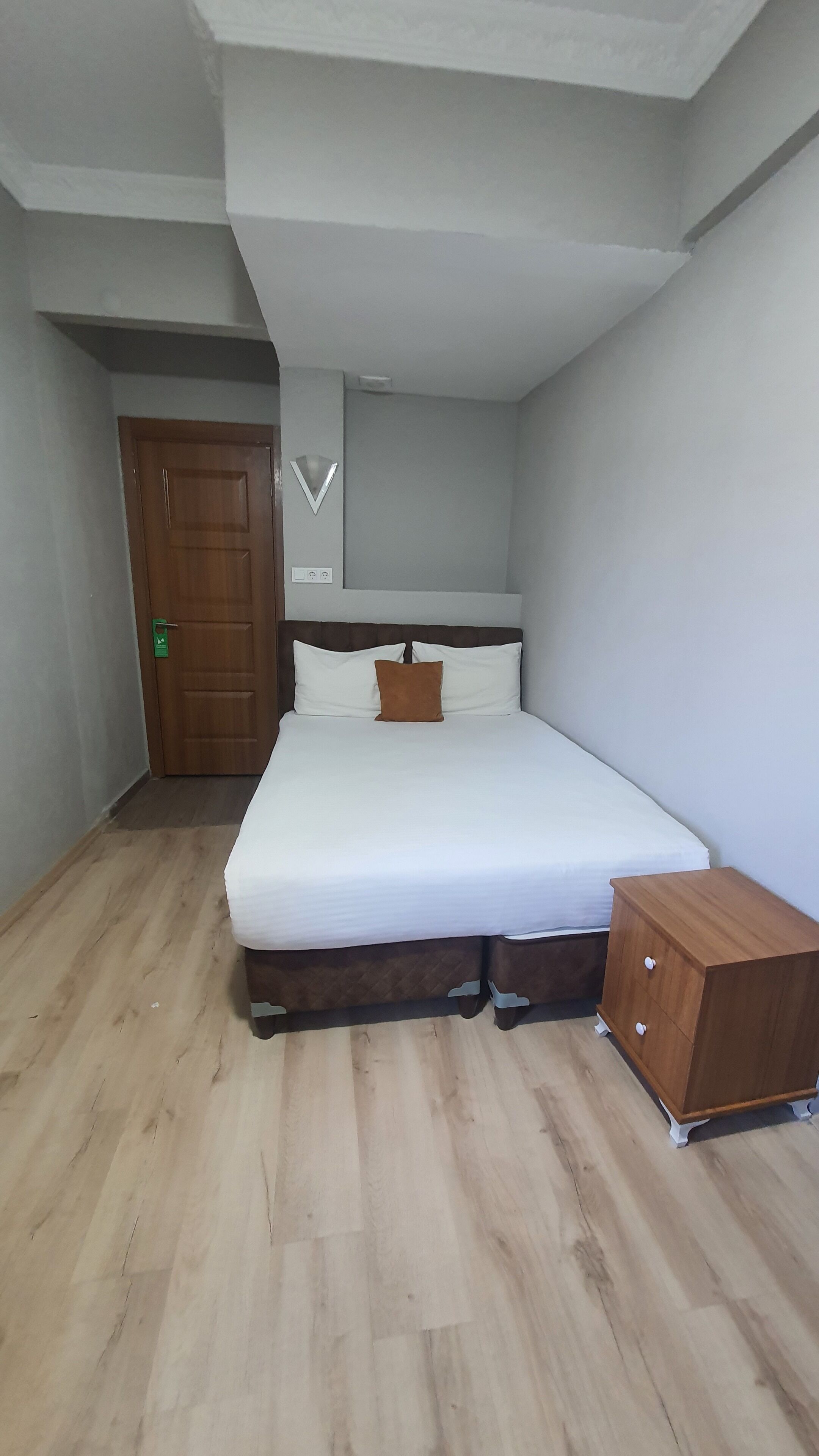 Um quarto com uma cama, uma mesinha de cabeceira de madeira e uma porta.