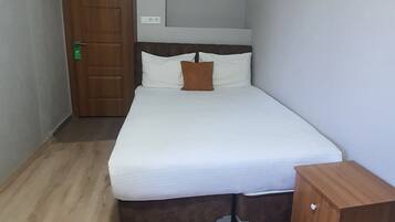 Um quarto com uma cama, uma mesinha de cabeceira de madeira e uma porta.