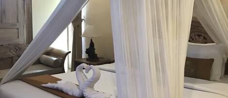 Uma cama de dossel com estrutura de madeira, um criado-mudo e uma toalha decorativa em formato de cisne.