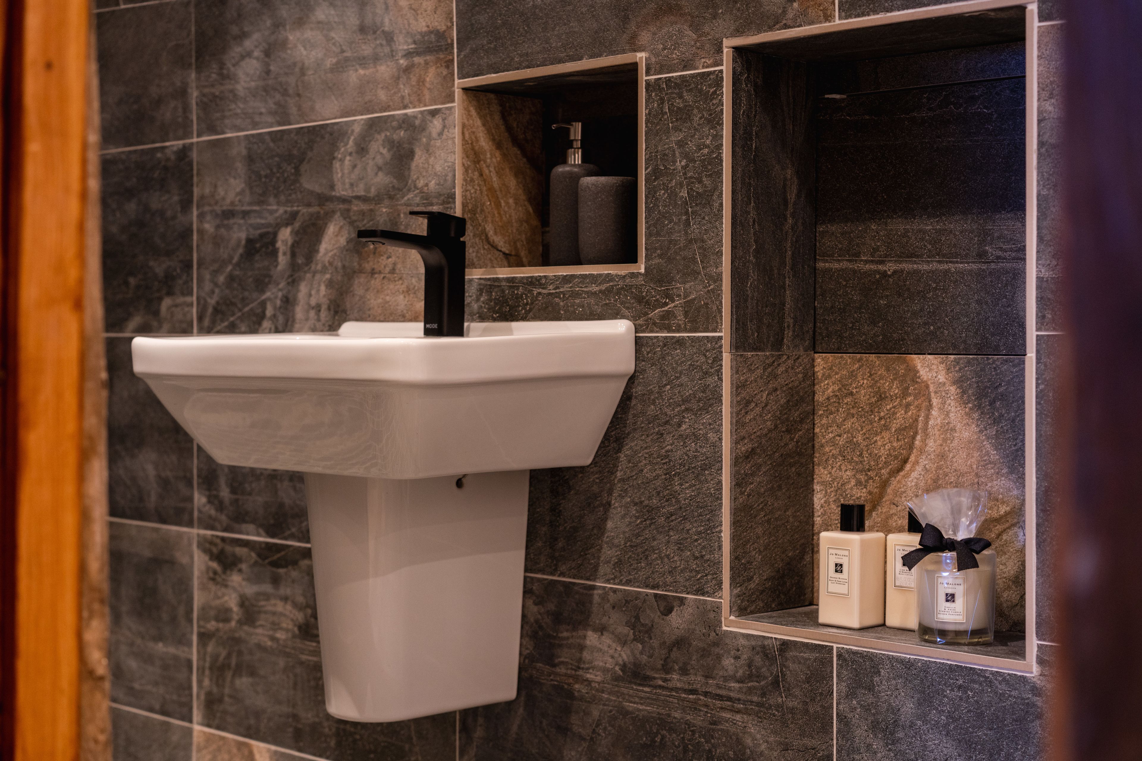 Casa de banho com lavatório pedestal branco, espelho e dois frascos de produtos de higiene numa prateleira.