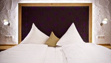 Cama bem arrumada com lençóis brancos e um único travesseiro decorativo, diante de uma parede texturizada com papel de parede estampado escuro.