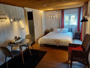 Quarto com cama, uma cadeira, uma mesinha e janela com cortinas.