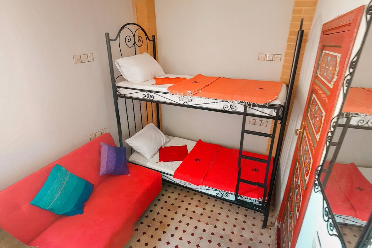 Quarto em dormitório com duas beliches, um sofá vermelho e um espelho.