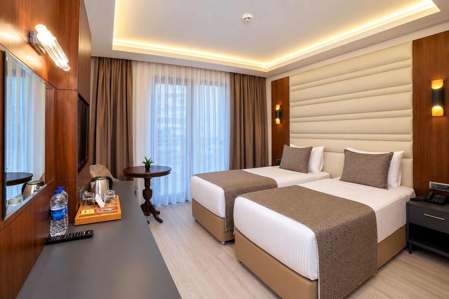 Quarto de hotel com duas camas, uma escrivaninha com um laptop, um minibar e vista da cidade através de amplas janelas.