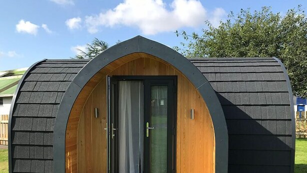 Uma cabana pequena de madeira, com arco, e exterior preto, com porta de vidro.