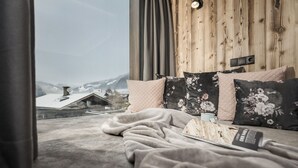 Quarto com vista para montanhas, parede de madeira e cama com almofadas florais.