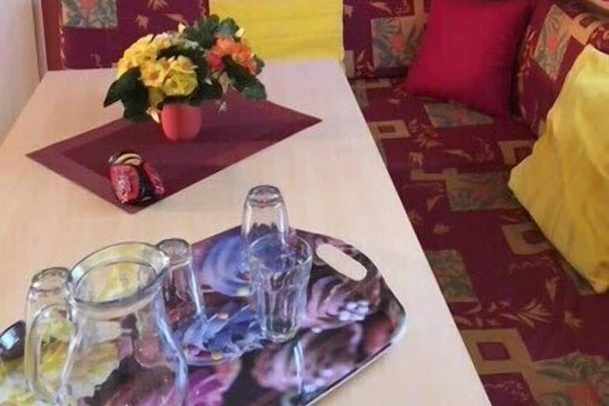 Uma área de refeições com uma mesa posta para dois, um sofá com almofadas estampadas e um vaso decorativo com flores.