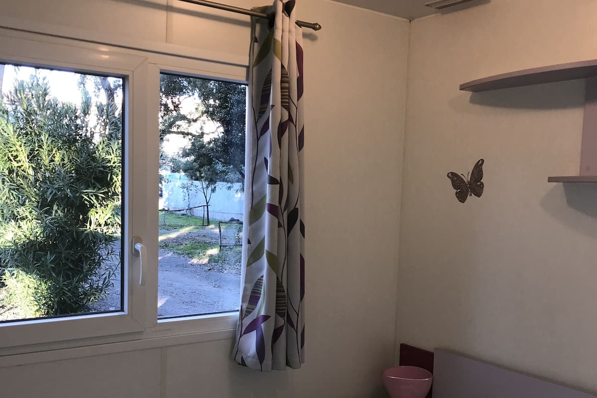 Quarto com cama, janela com cortinas, uma tigela rosa e decoração de borboleta na parede.