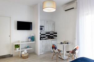 Um espaço compacto com cozinha compacta, televisão de tela plana, área de refeições com duas cadeiras e uma janela grande com cortinas.
