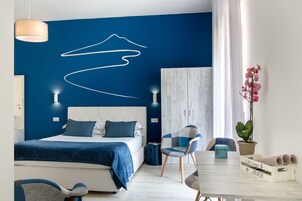Quarto moderno com cama, mesas de cabeceira, uma cadeira, uma mesinha e um vaso com planta.