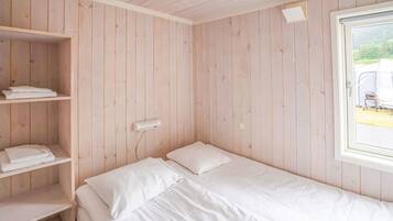 Um quarto de madeira com uma cama, prateleiras e uma janela.