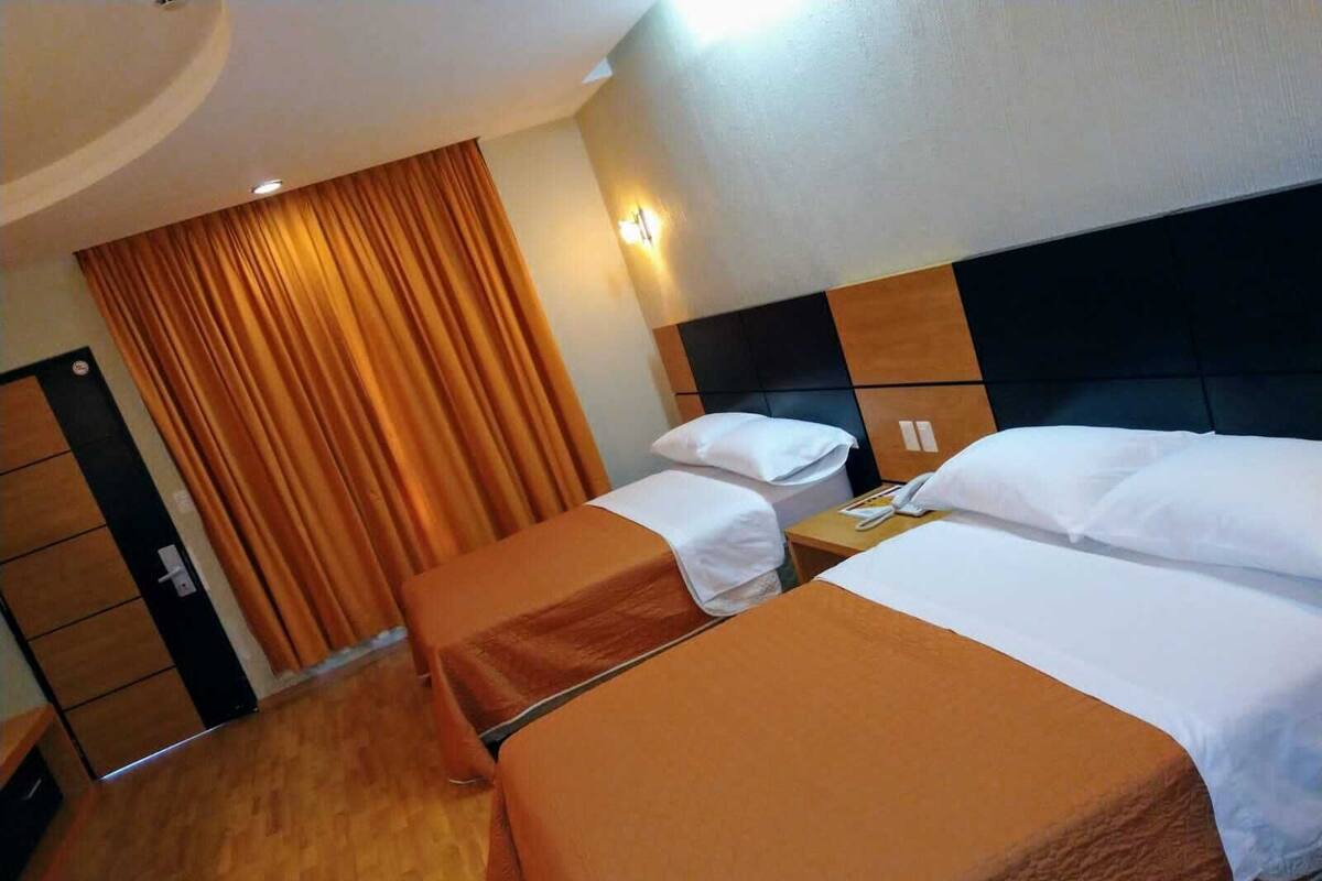 Quarto de hotel com duas camas, piso de madeira, cabeceira e cortina.