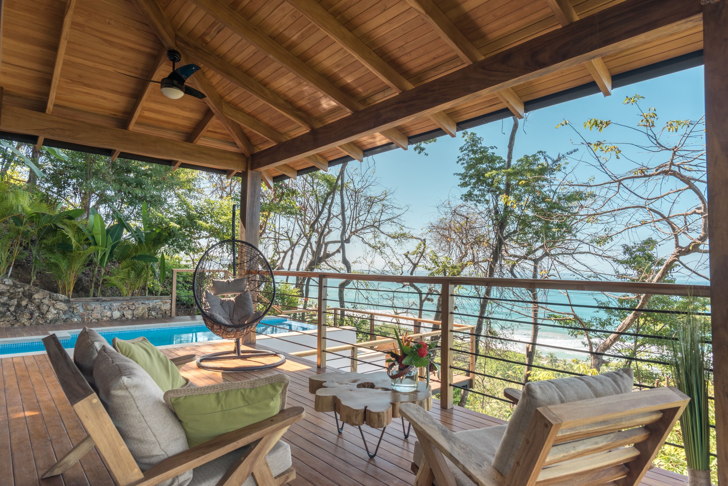 Um deck de madeira com piscina, área de estar externa e vista para a praia.