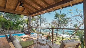 Um deck de madeira com piscina, área de estar externa e vista para a praia.