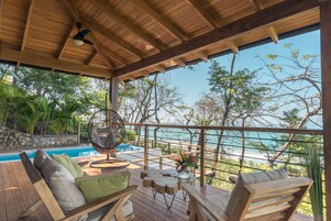 Um deck de madeira com piscina, área de estar externa e vista para a praia.