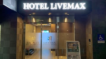 Entrada do Hotel Livemax, com placa visível, sinalização de acessibilidade para cadeiras de rodas e painel digital.