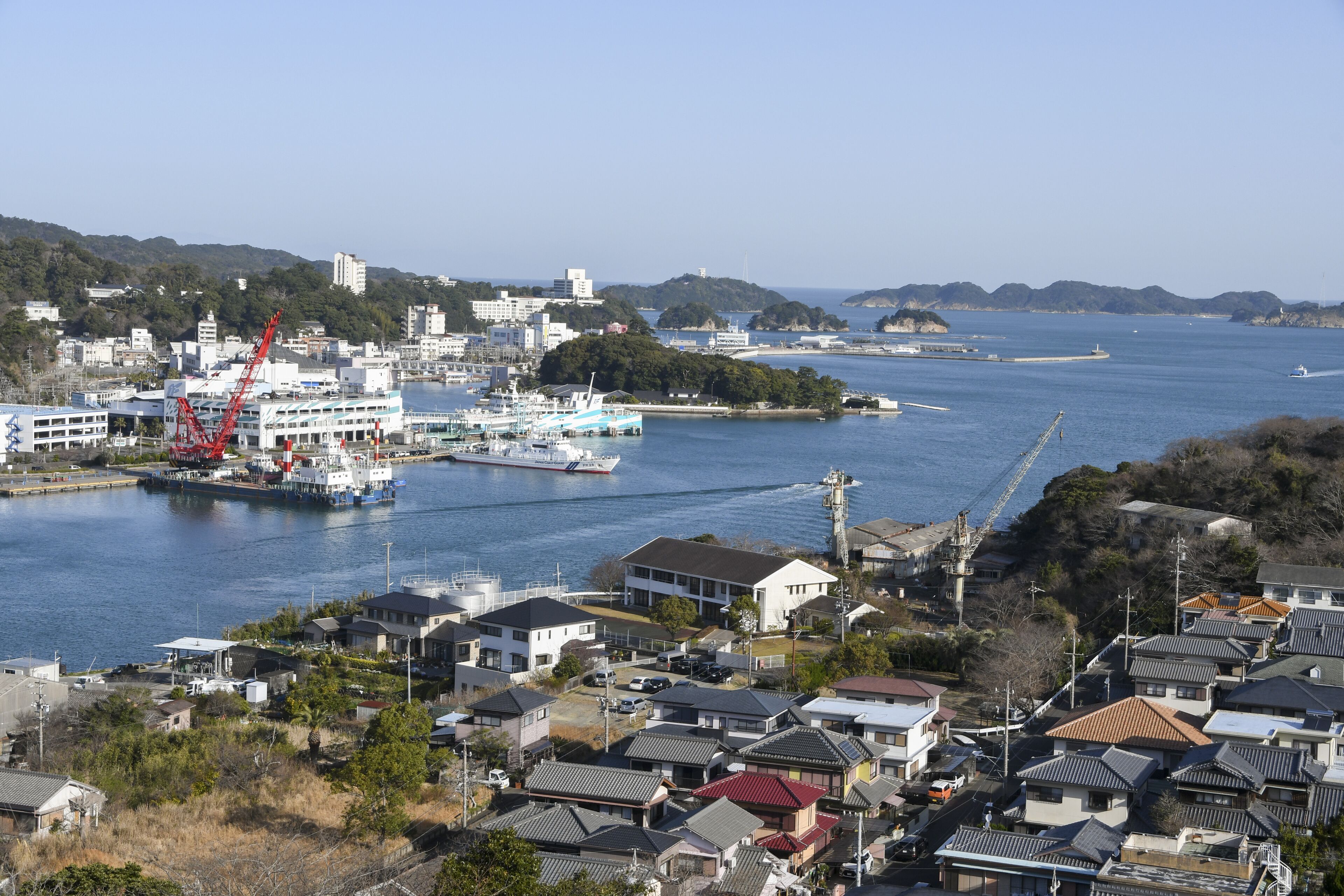 Uma vila costeira com edifícios residenciais, um cais de ferry e uma ponte.