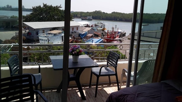 Uma varanda com mesa e cadeiras, um vaso de flores e vista para um cais com barcos e edifícios do outro lado da água.