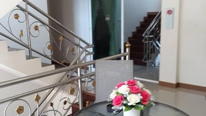 Um interior moderno com mesa de vidro, guarda-corpo metálico, escada e porta que dá acesso a outro espaço.