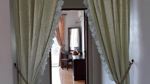 Um corredor com uma porta que dá para um quarto. O corredor possui piso de azulejos e cortinas com franjas nas laterais.