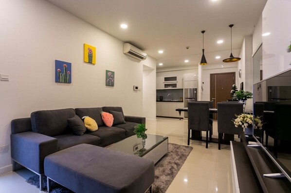 Uma sala de estar moderna com um sofá cinza escuro, uma mesa de centro de vidro e um espaço de jantar com cadeiras pretas.