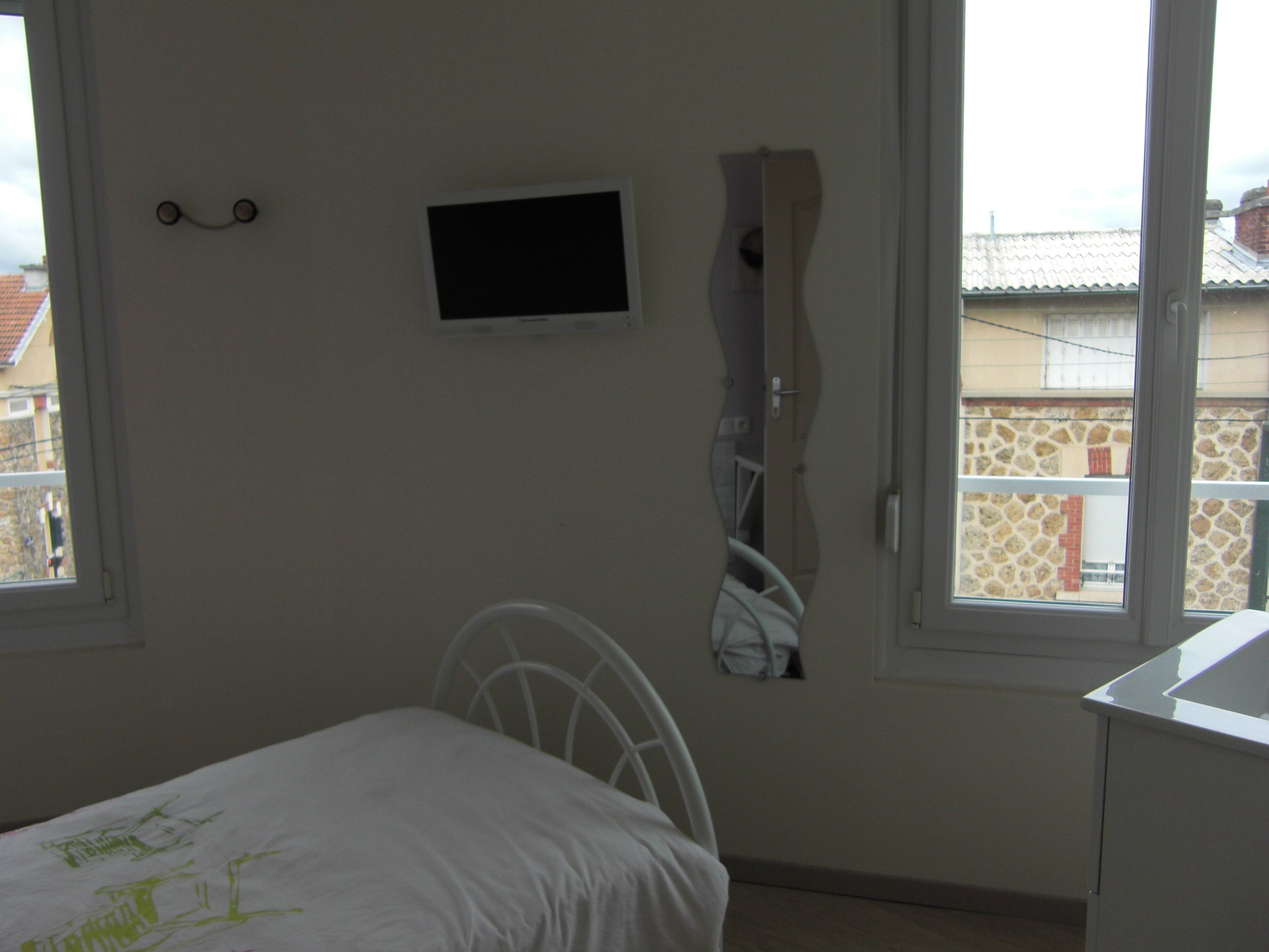 Quarto com cama, televisão na parede e janela com vista para edifícios.