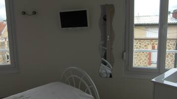 Quarto com cama, televisão na parede e janela com vista para edifícios.
